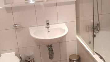Casa de banho com lavatório branco, espelho e cabine de duche em vidro.