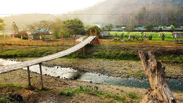 Uma ponte de madeira rústica sobre um riacho, cercada por vegetação e um fundo com névoa.