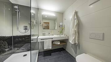 Um banheiro moderno com chuveiro em cabine de vidro, pia branca com espelho, vaso sanitário e porta-toalhas.