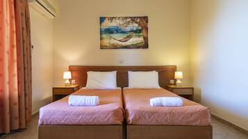 Quarto de hotel com duas camas, um quadro de uma paisagem praiana e uma janela com cortinas.