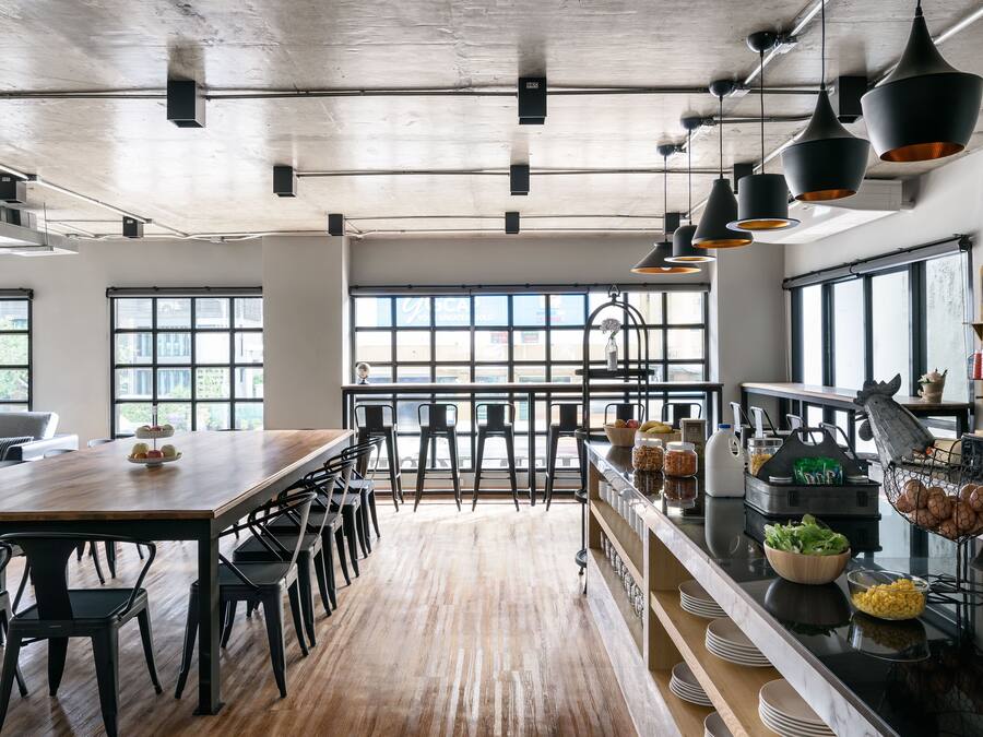 Uma cozinha ampla com uma longa mesa de madeira, banquetas de bar e iluminação pendente moderna.