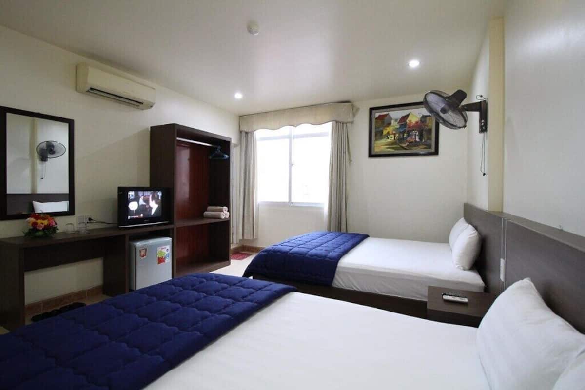 Quarto de hotel com duas camas, uma escrivaninha com televisão, ar condicionado e uma janela com cortinas.