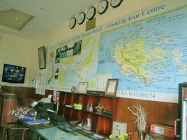 Um balcão de reservas com um mapa grande, relógios, um computador e uma mesa com telefone.