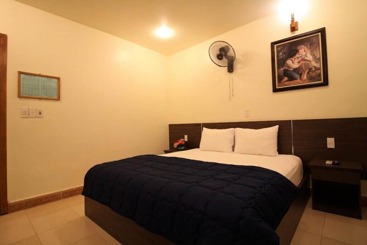 Quarto de hotel com cama grande, mesa de cabeceira, ventoinha fixada na parede, um quadro e um mural.