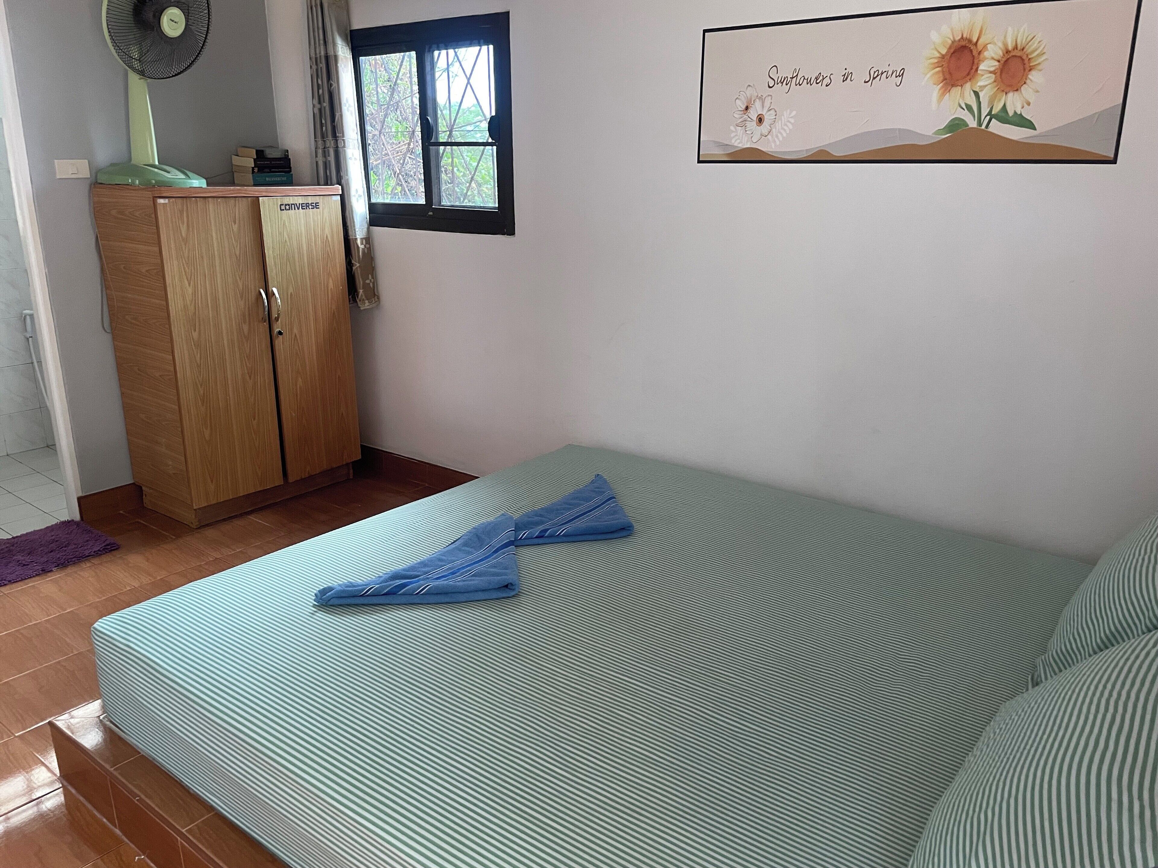 Quarto com cama, guarda-roupa de madeira, janela e um adorno na parede.