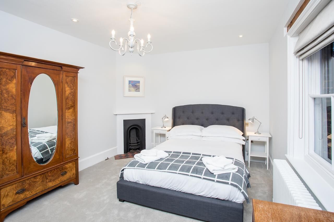 Quarto com uma cama grande, guarda-roupa de madeira, lareira e janela com cortinas.