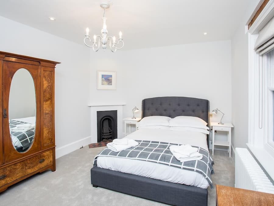 Quarto com uma cama grande, guarda-roupa de madeira, lareira e janela com cortinas.