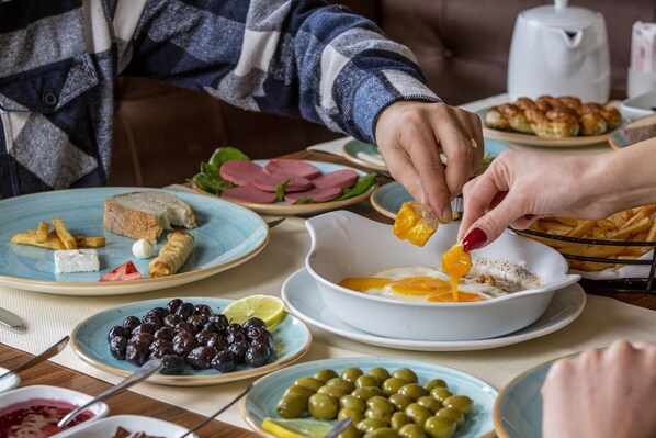 Uma mesa de jantar com diversos pratos, incluindo pão, ovos, azeitonas e um prato de carne.