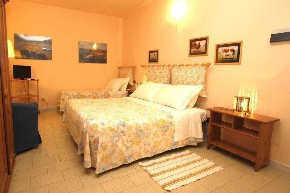 Quarto com duas camas, uma mesa de cabeceira de madeira e uma televisão presa à parede.