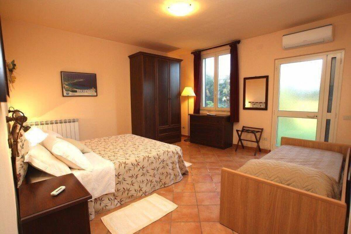 Quarto com duas camas, uma mesa de cabeceira, luminária, janela e um quadro na parede.
