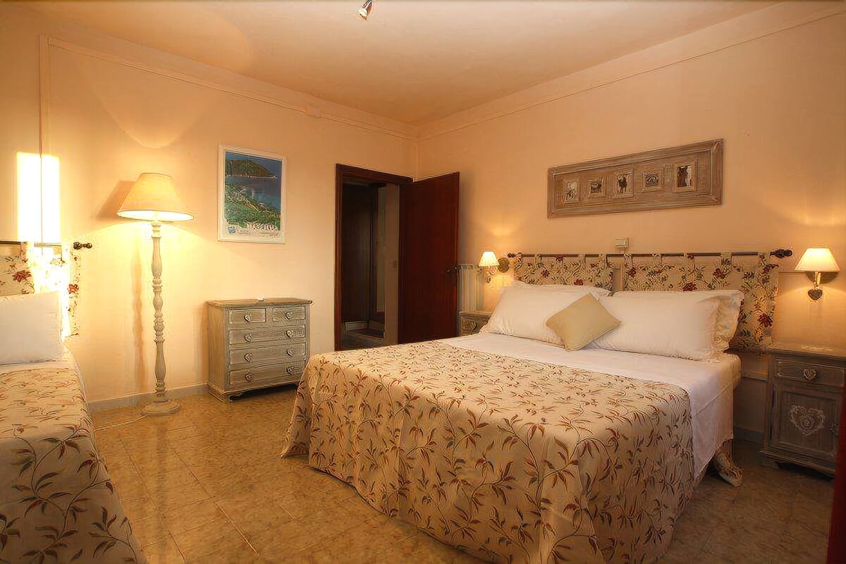 Quarto de hotel com uma cama grande, duas mesas de cabeceira com abajures, um penteado e uma porta que dá para outro quarto.