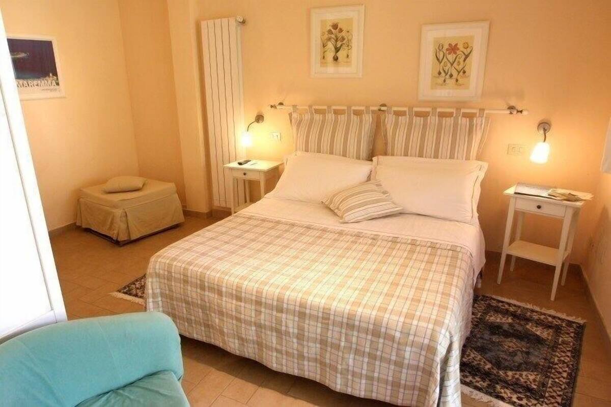 Quarto com cama, mesas de cabeceira, uma cadeira e radiador.