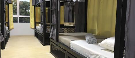 Quarto estilo dormitório com beliches, janela e cortinas.