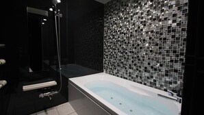 Uma casa de banho moderna com chuveiro em cabine de vidro, uma banheira independente e uma parede com mosaico escuro.