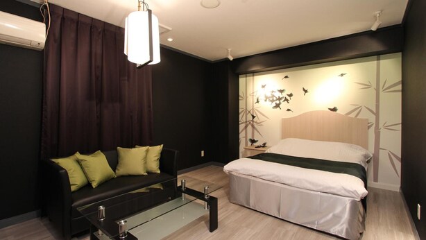 Quarto moderno com sofá preto, mesa de centro de vidro, cama com cabeceira de madeira e parede com design em bambu.