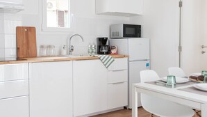 Uma cozinha moderna com armários brancos, bancada de madeira, micro-ondas, máquina de café e uma área de refeições com mesa e cadeiras.