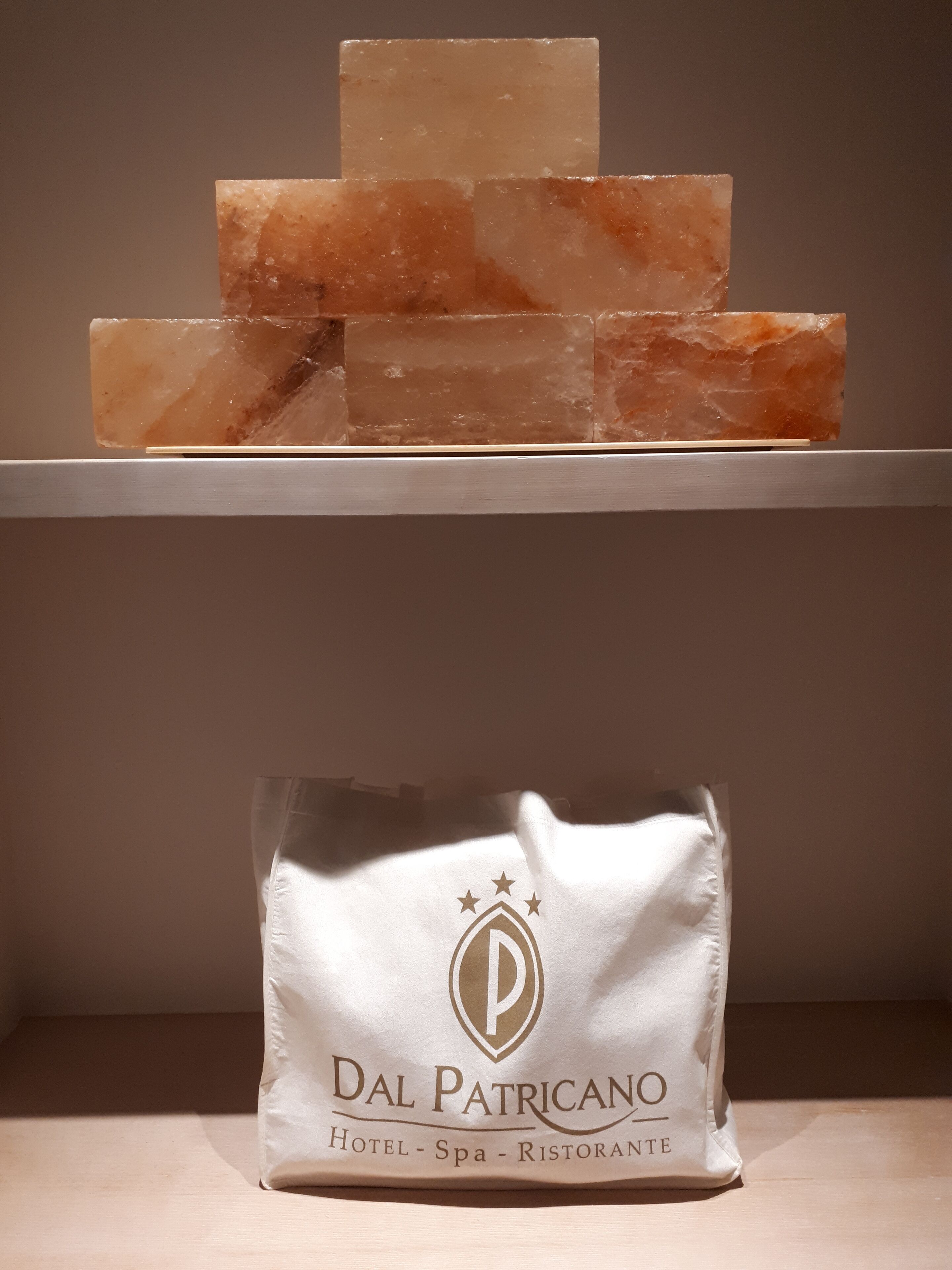 Almofada branca com o logotipo e o nome 'Dal Patricano Hotel - Spa - Ristorante' sobre uma superfície de madeira.