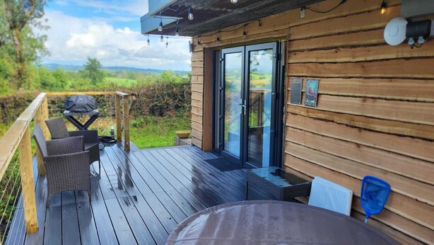 Um deck de madeira com móveis externos, churrasqueira e porta de vidro que dá para um quarto.