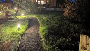 Um caminho leva a uma casa com fachada de madeira, cercada por grama e árvores.
