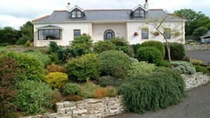 Uma casa de dois andares com um jardim murado de pedra e telhado inclinado.