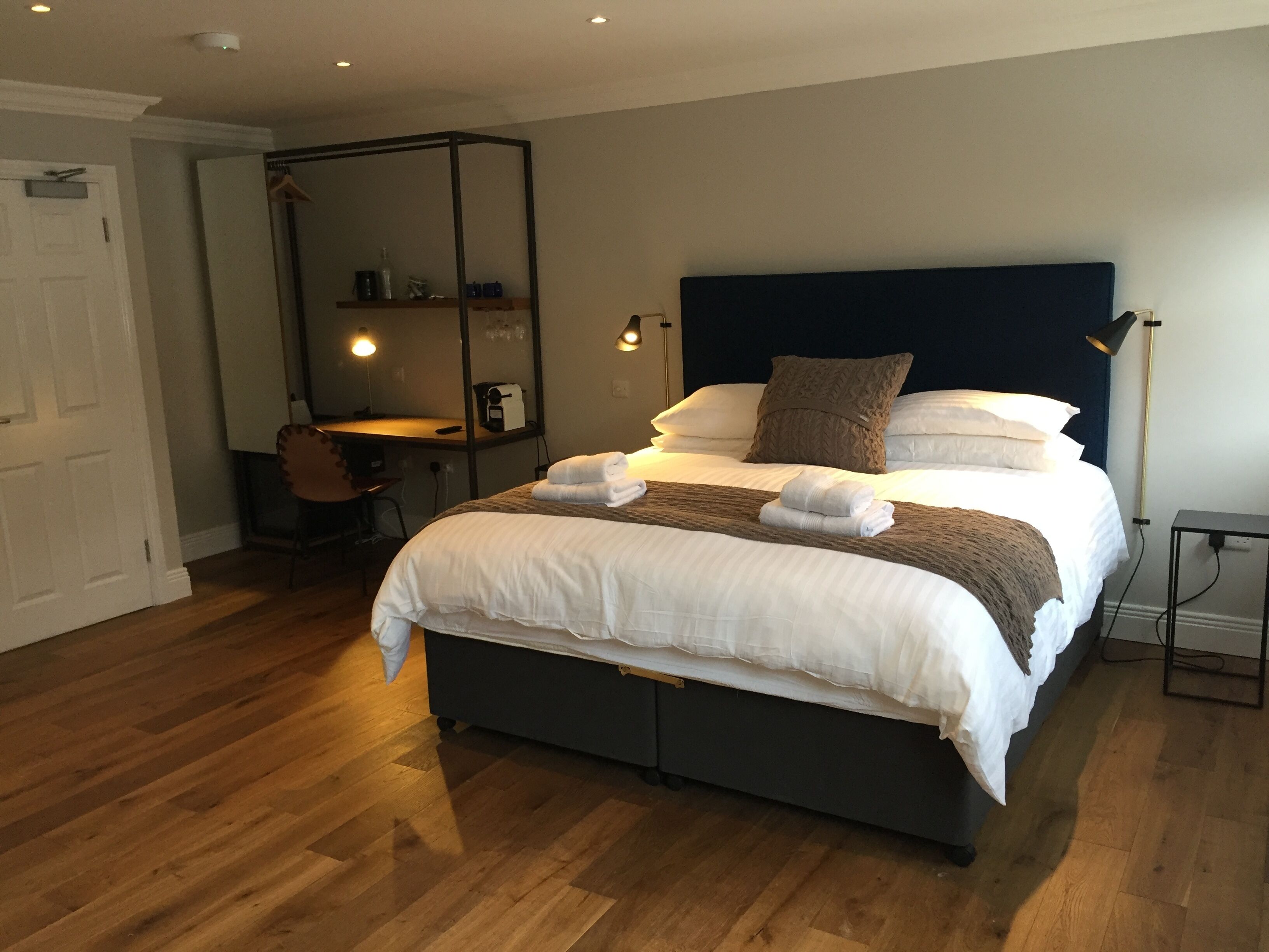 Quarto de hotel com uma cama grande, uma escrivaninha, uma cadeira e um espelho.