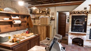 Uma cozinha com arco de pedra, prateleiras de madeira, forno a pizza e um fatiador de carne.