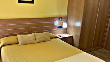 Quarto de hotel com cama grande, cabeceira de madeira, mesa de cabeceira com abajur e um quadro na parede.