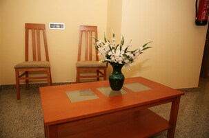 Mesa de madeira com um vaso de flores brancas, duas cadeiras de madeira com almofadas e uma tomada elétrica na parede.