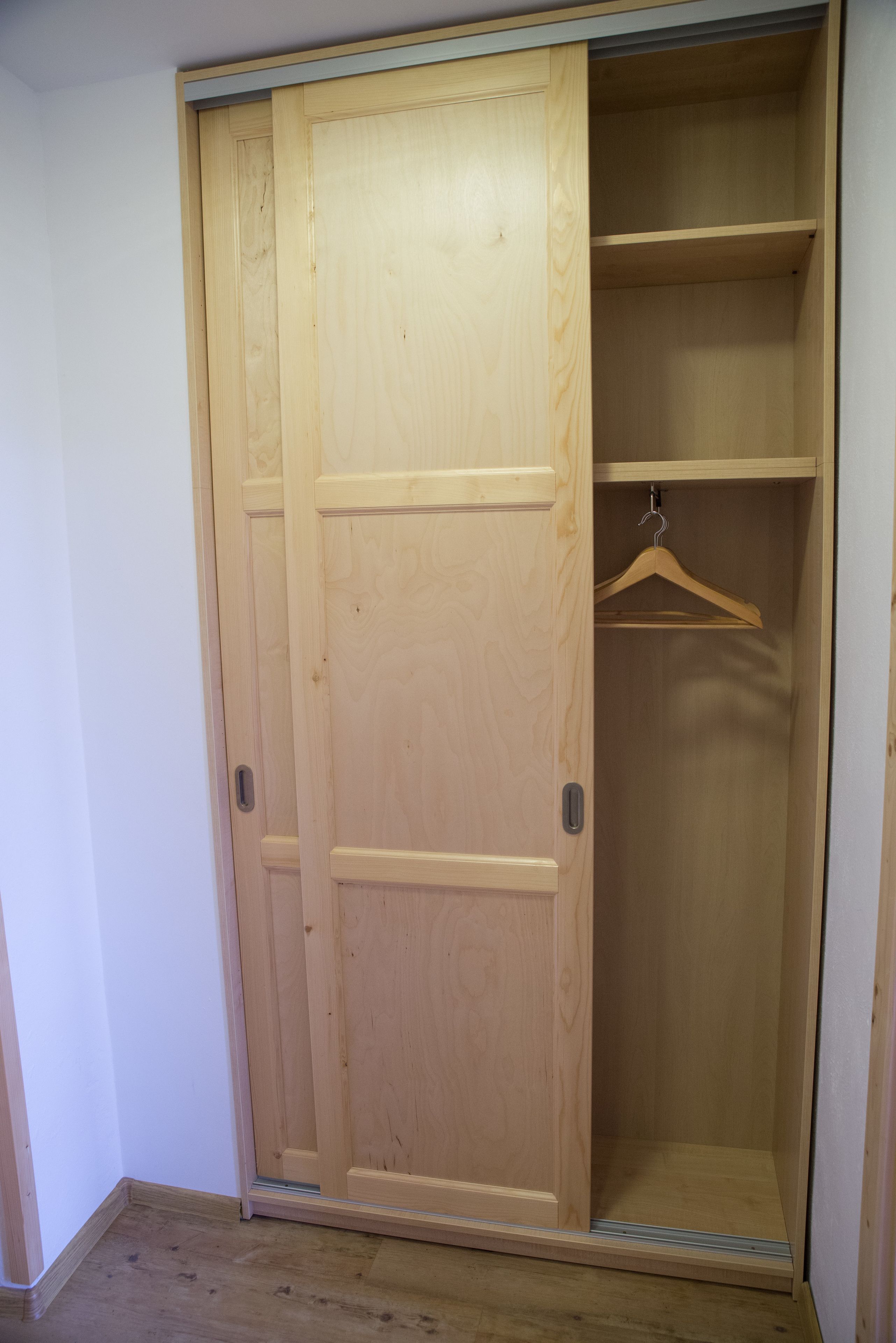 Um guarda-roupa de madeira com porta deslizante, barra para pendurar roupas e prateleira.