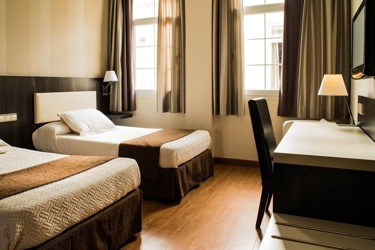 Quarto de hotel com duas camas, uma mesa e uma cadeira.