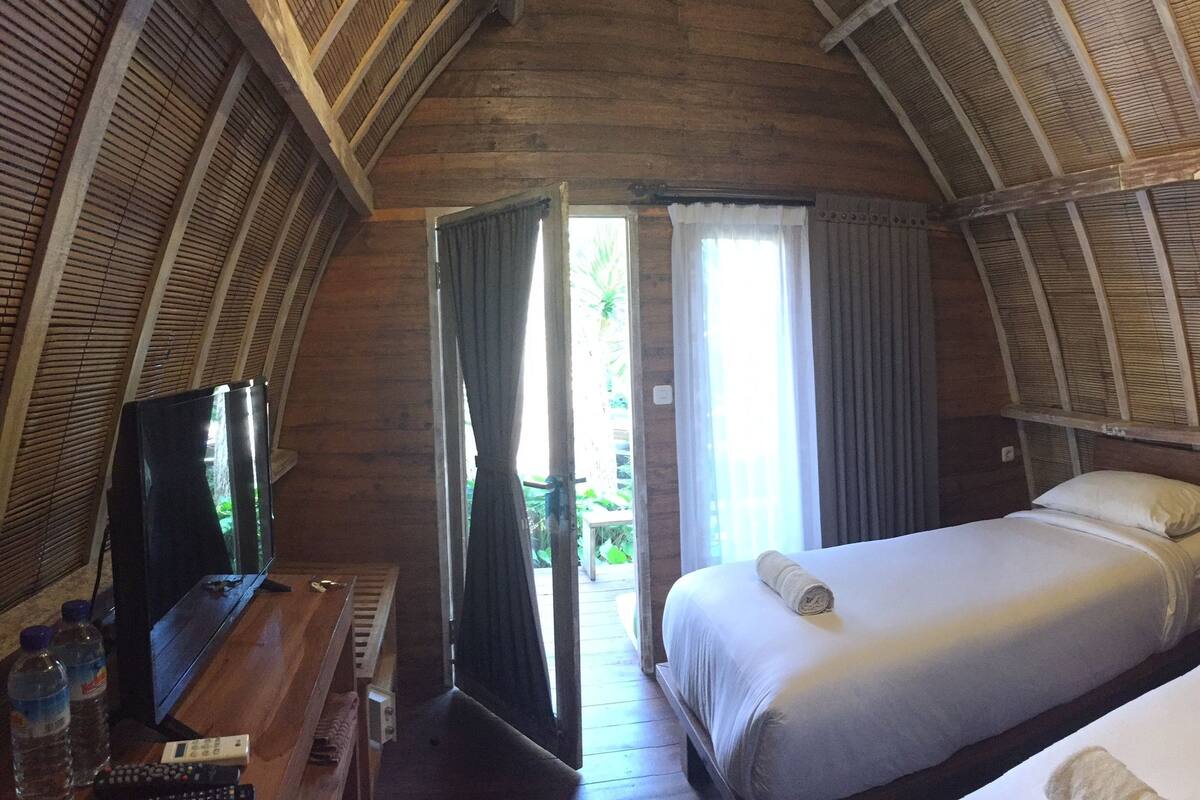 Quarto com duas camas, televisão e teto de madeira.