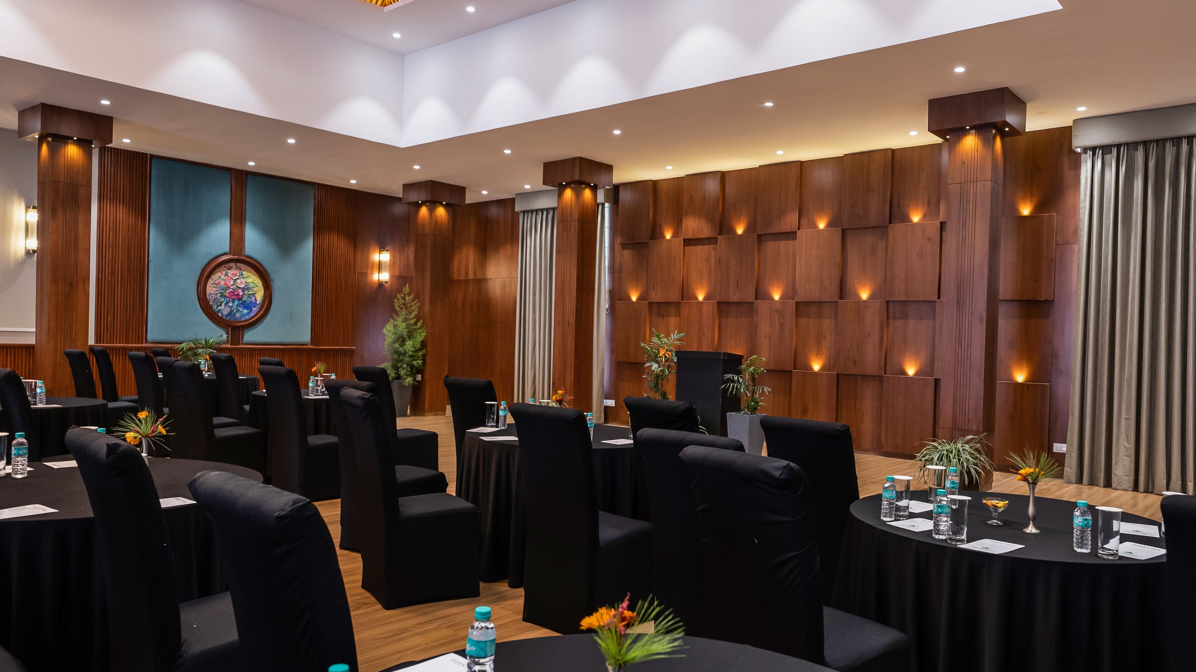 Uma sala de conferências com várias mesas e cadeiras, paredes de painel de madeira e iluminação embutida.