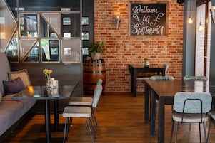 Um café acolhedor com parede de tijolos, um letreiro de boas-vindas e diversos tipos de assentos, incluindo um sofá, mesas e cadeiras.