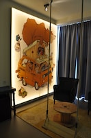 Quarto com um grande mural de um caminhão de desenho animado, uma poltrona preta e uma pequena mesa de madeira.
