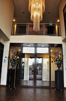 Entrada de hotel com portas duplas, um candelabro e dois arranjos florais.