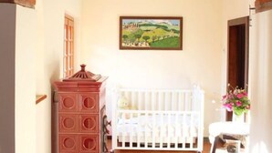 Um corredor com um arco de tijolos, um berço branco, um armário vermelho e um quadro na parede.