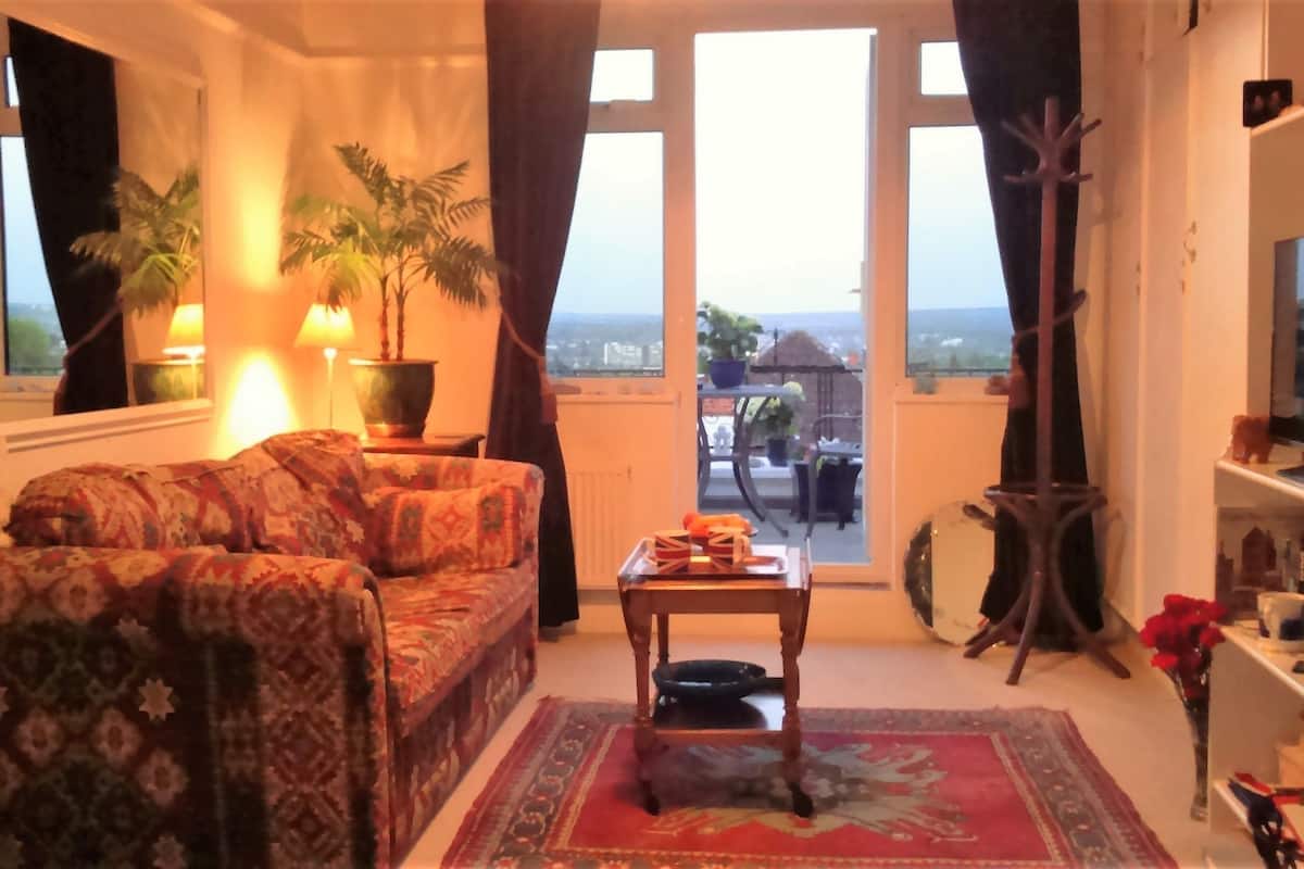 Uma sala de estar com um sofá, uma mesa de centro e vista para o exterior através de grandes janelas.