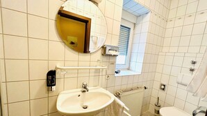 Casa de banho com lavatório branco, espelho e sanita.