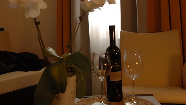 Uma mesa com uma orquídea em vaso, uma garrafa de vinho e dois copos de vinho sobre um jogo americano.