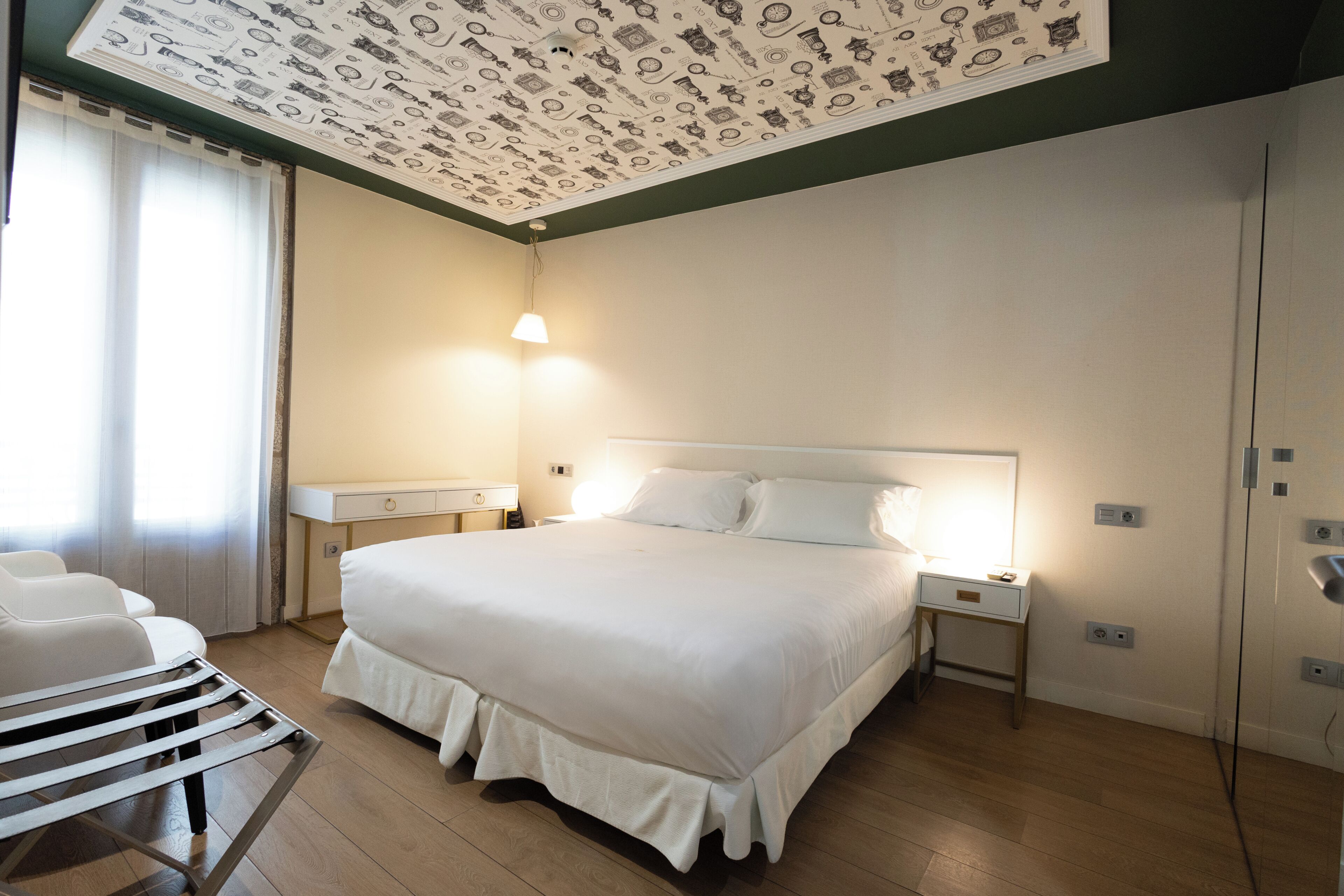 Quarto com uma cama grande, mesas de cabeceira, escrivaninha e uma cadeira.