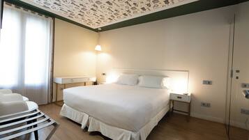 Quarto com uma cama grande, mesas de cabeceira, escrivaninha e uma cadeira.