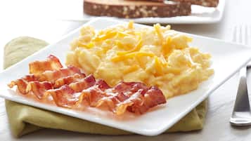 Um prato de ovos mexidos com queijo e bacon, acompanhado por duas fatias de torradas em um prato branco.