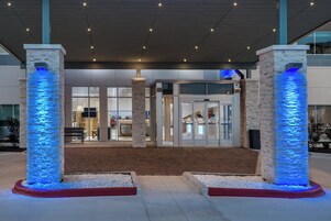 Entrada de hotel com design moderno, fachada em tijolos e pilares iluminados.