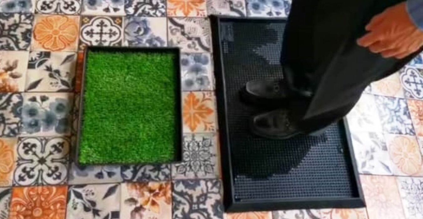 Piso ladrilhado com um tapete de grama sintética verde e um tapete texturizado preto.