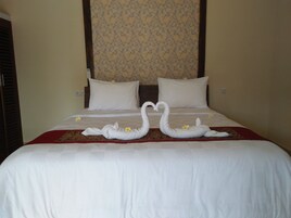 Quarto de hotel com cama bem arrumada, duas almofadas e parede com padrão floral.