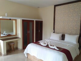 Quarto de hotel com cama, espelho, guarda-roupa e um banquinho.