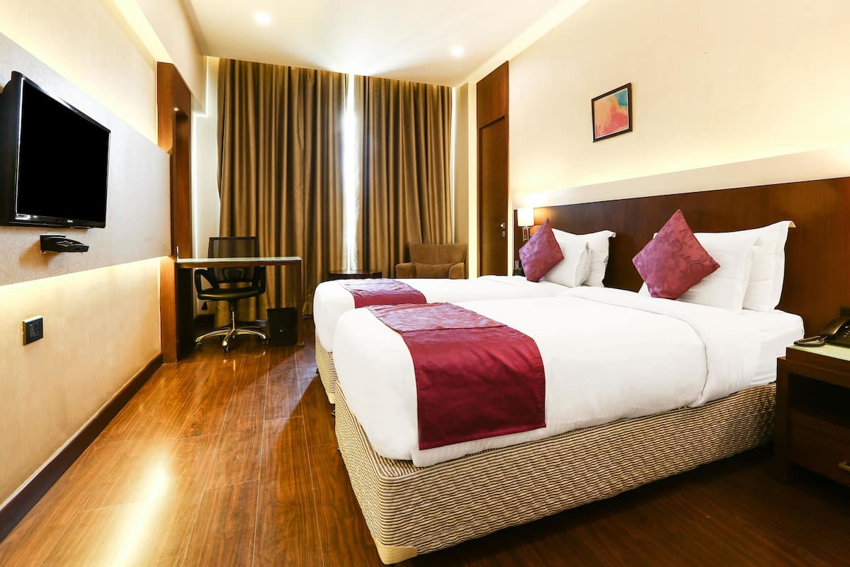 Quarto de hotel com uma cama grande, uma escrivaninha, uma cadeira, uma televisão e uma janela com cortinas.
