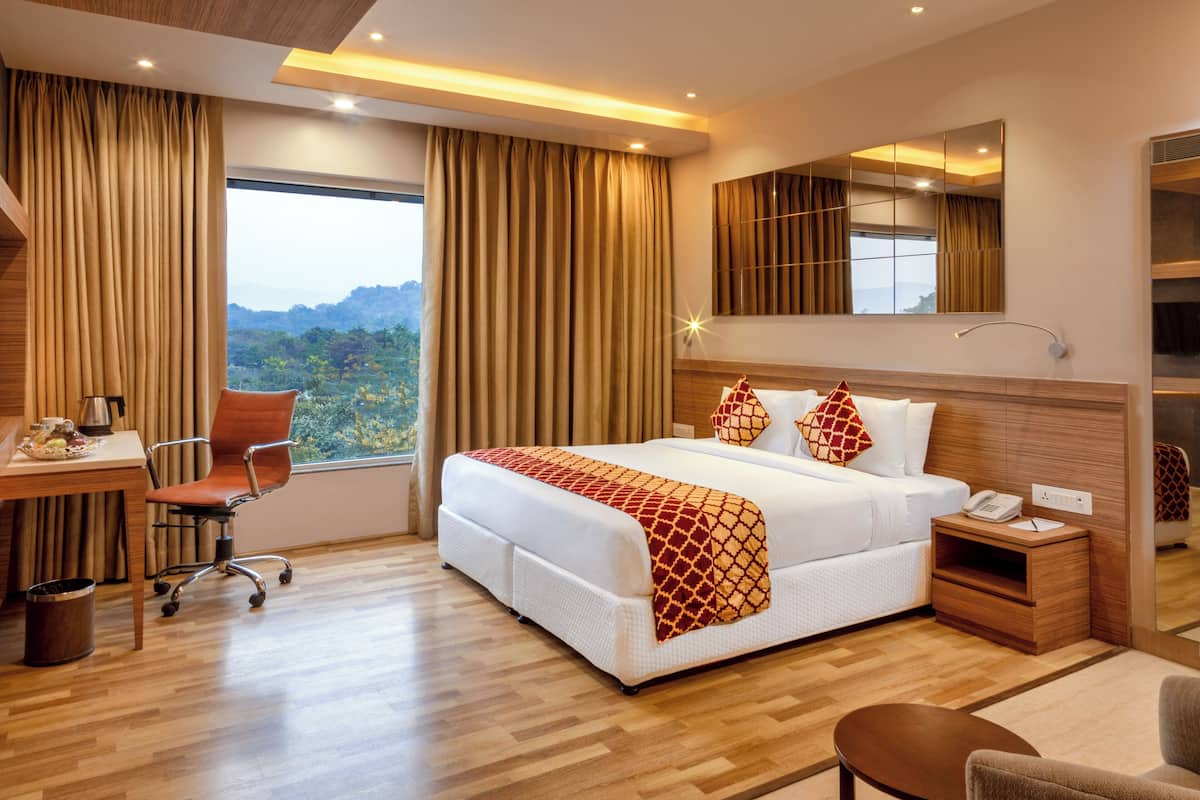 Quarto de hotel moderno com uma cama grande, uma escrivaninha com cadeira, uma mesinha e vista para o exterior.