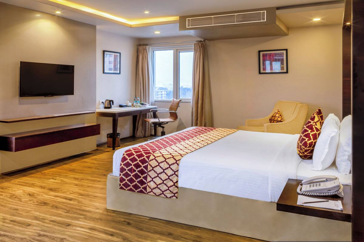 Quarto de hotel com uma cama grande, uma escrivaninha com cadeira, televisão e janela com cortinas.