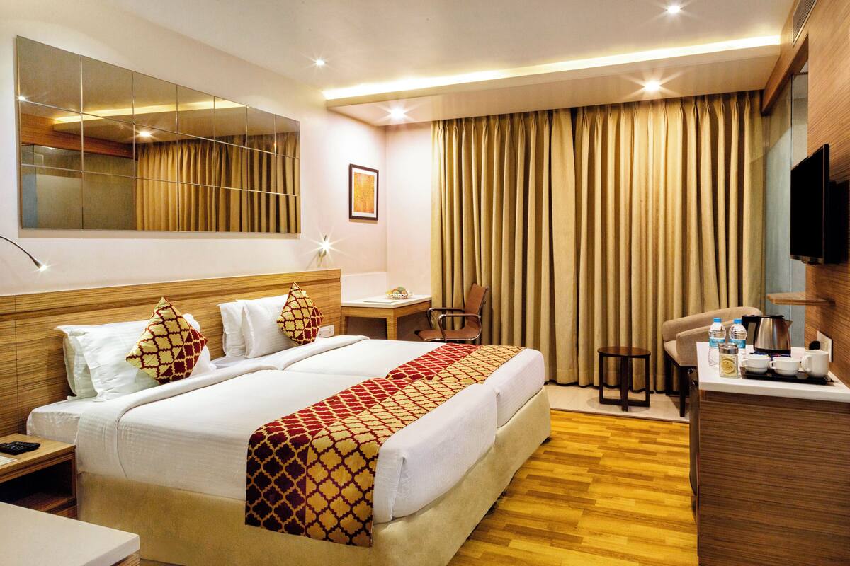 Quarto de hotel com uma cama grande, uma escrivaninha, uma cadeira, uma televisão e um espelho.